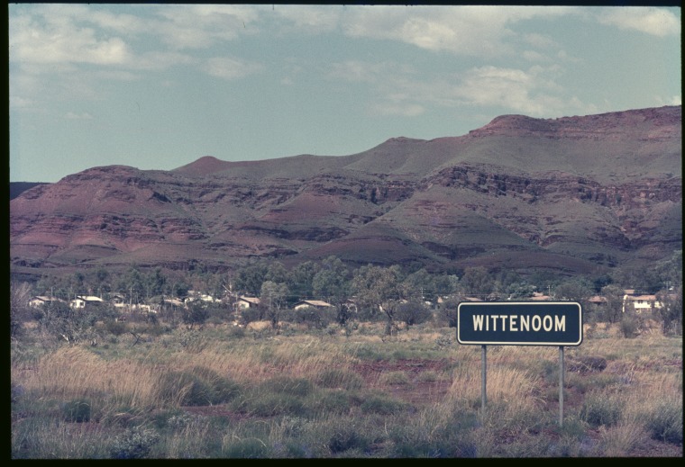 Sign for Wittenoom, with the town and the Hamersley Range behind ...